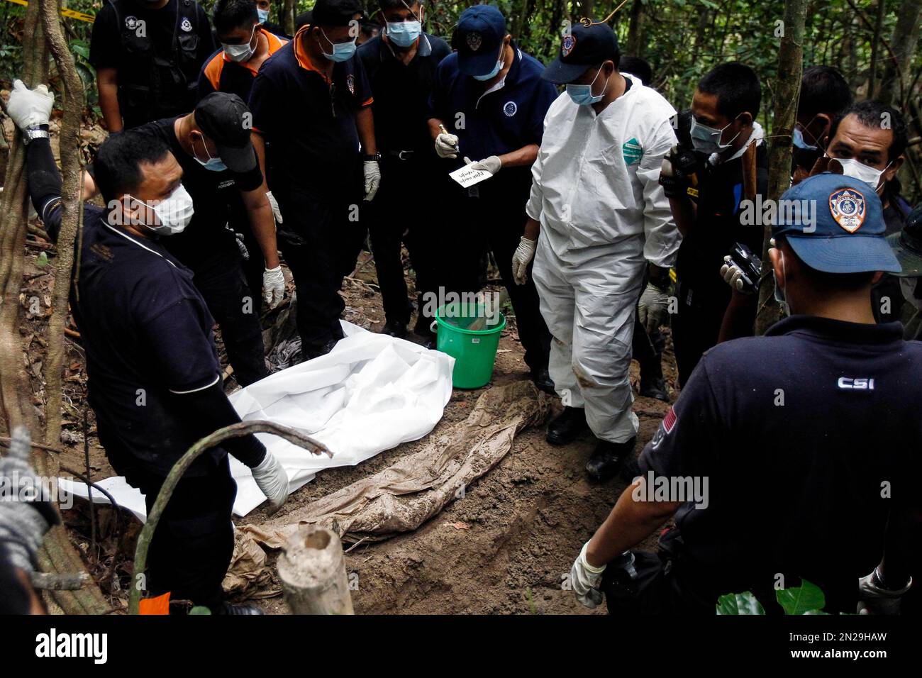 Malaysian police forensic team members inspect a freshly exhumed human ...
