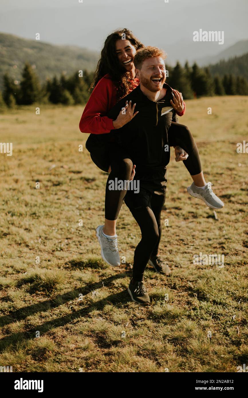 Pretty young woman riding piggyback on a boyfriend at green hills Stock ...