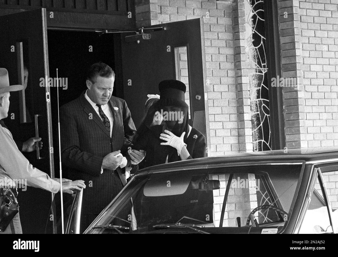 Faith Clark Freeman, wearing veiled hat, is assisted by a church usher ...