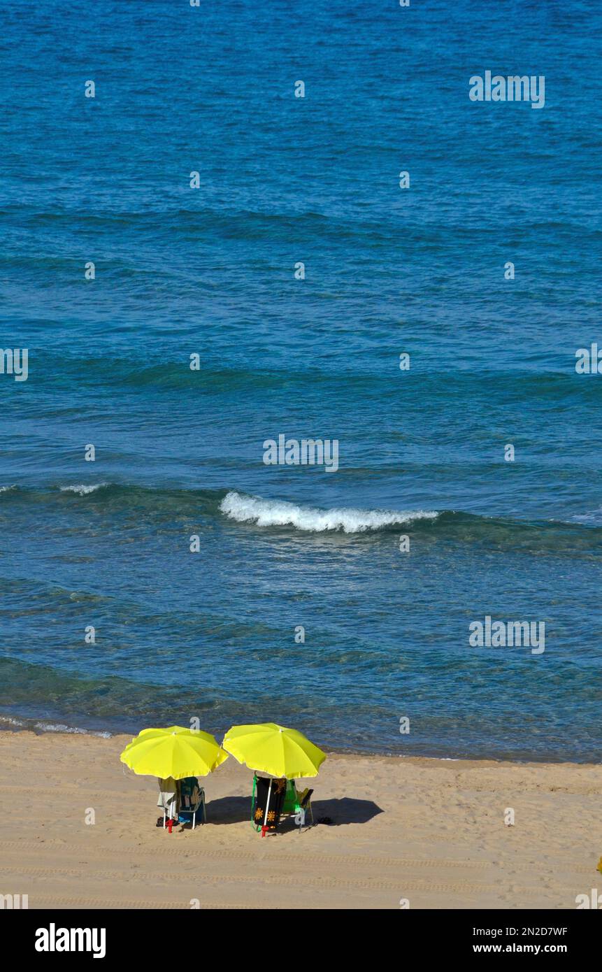 Beachgoers under yellow umbrellas by the sea with wave, Hospitalet ...