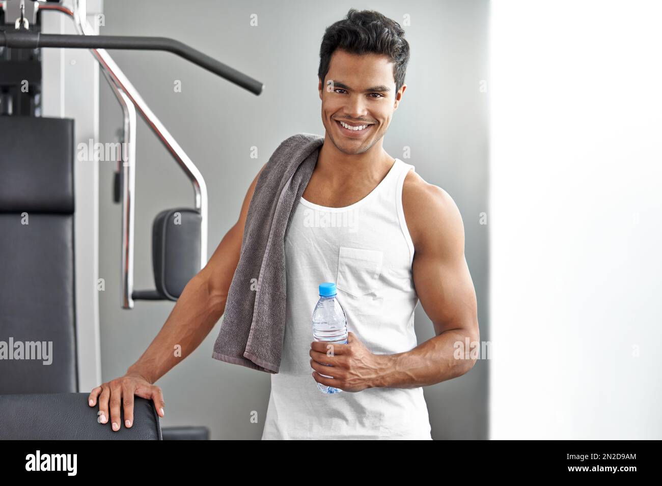 Gym is my life. A young ethnic man standing by an exercise machine at ...