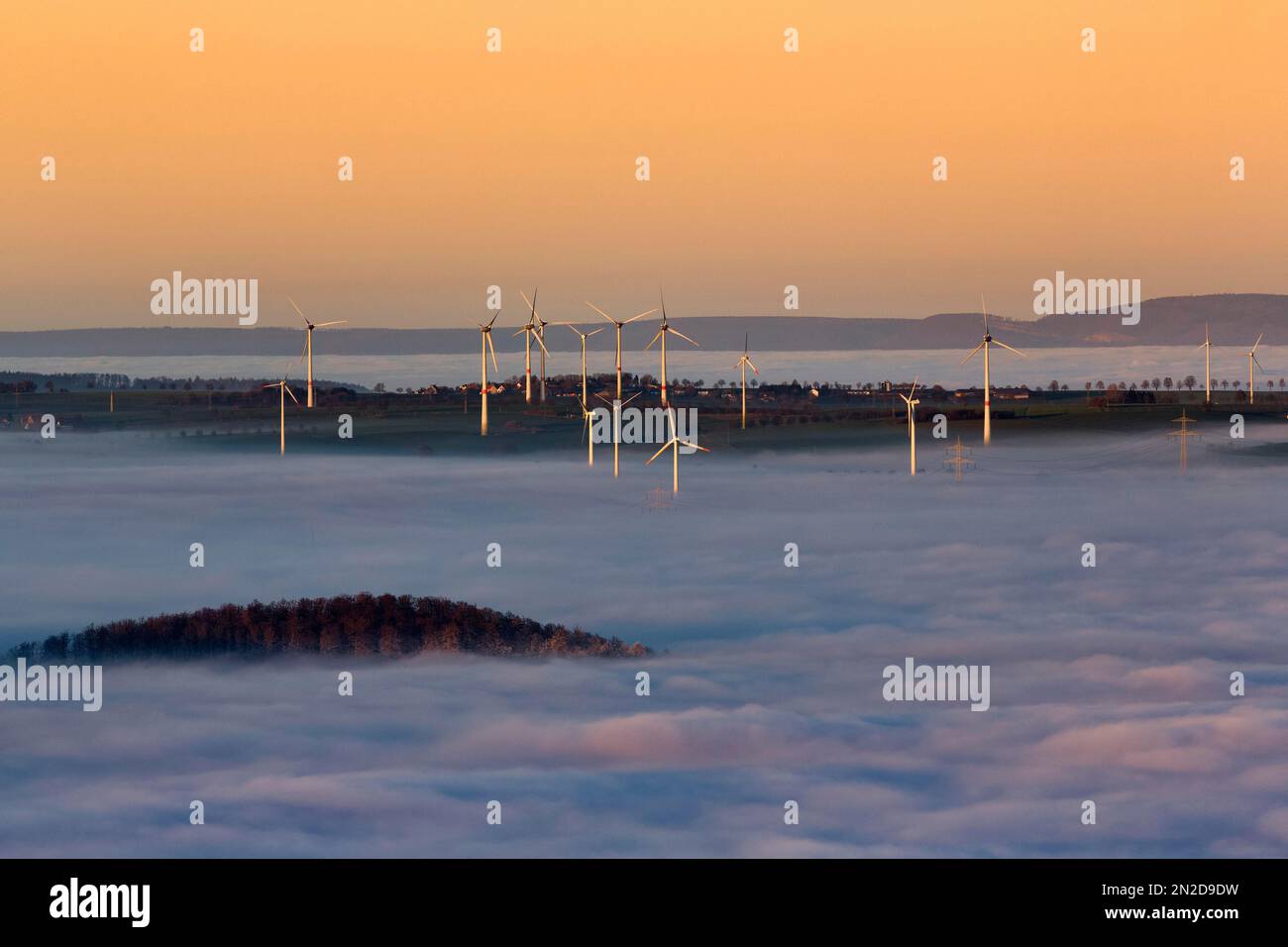 Wind turbines illuminated by the sun and forest rising from cloud cover ...
