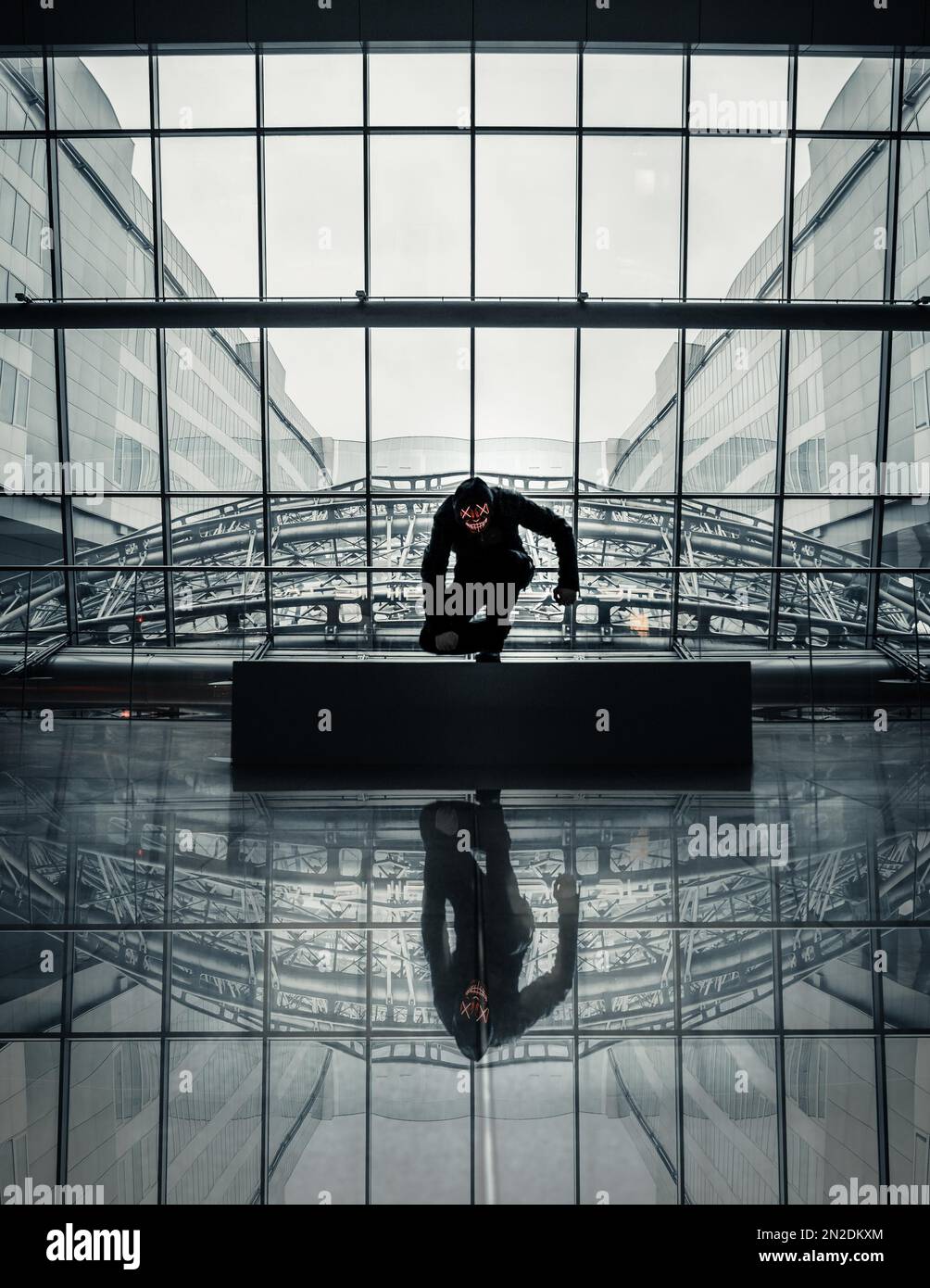 Man with Purge mask in a modern building, kneeling and reflected in the ...