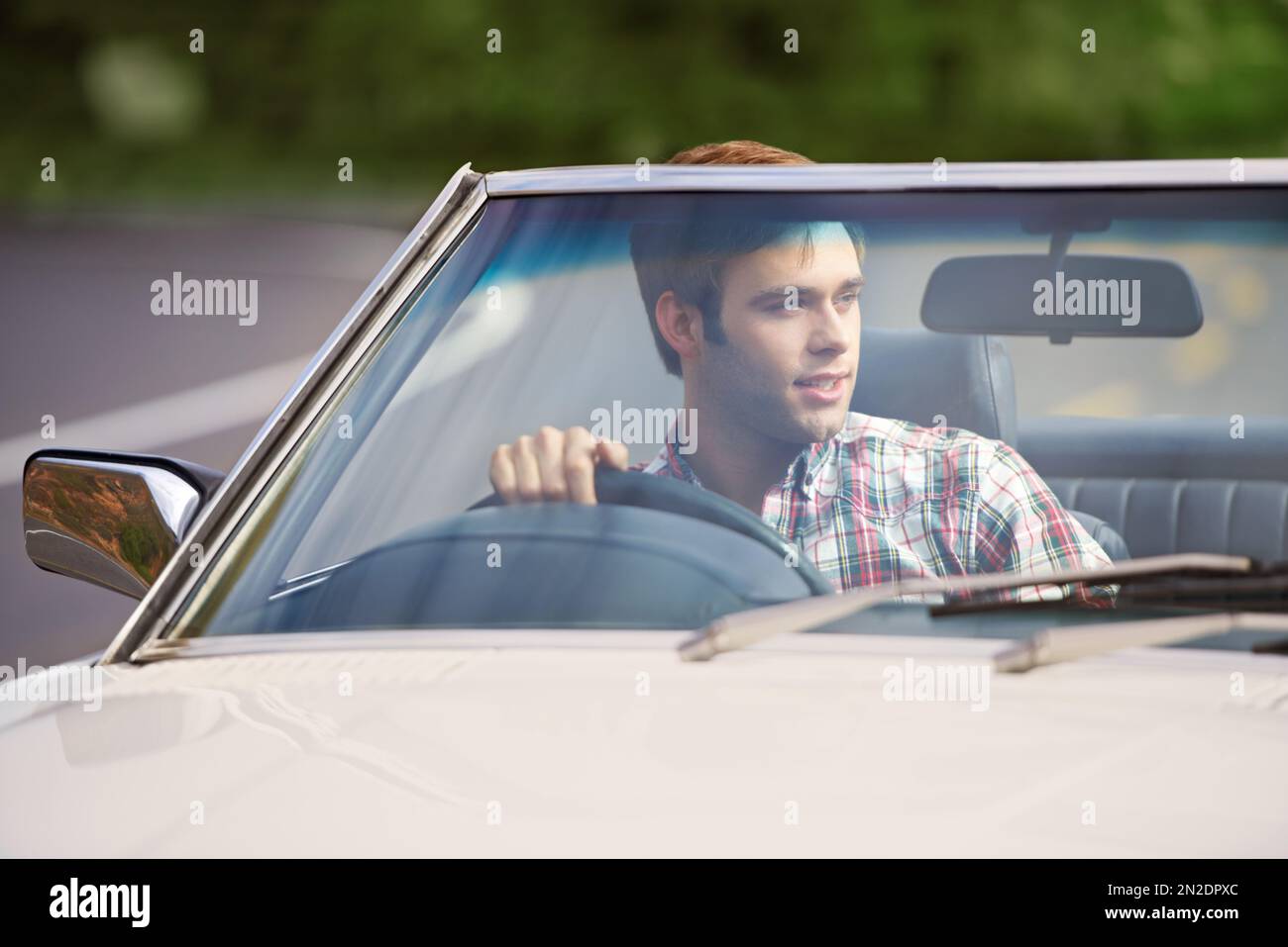 Freedom of the open road. a young man happily driving down a rural road ...