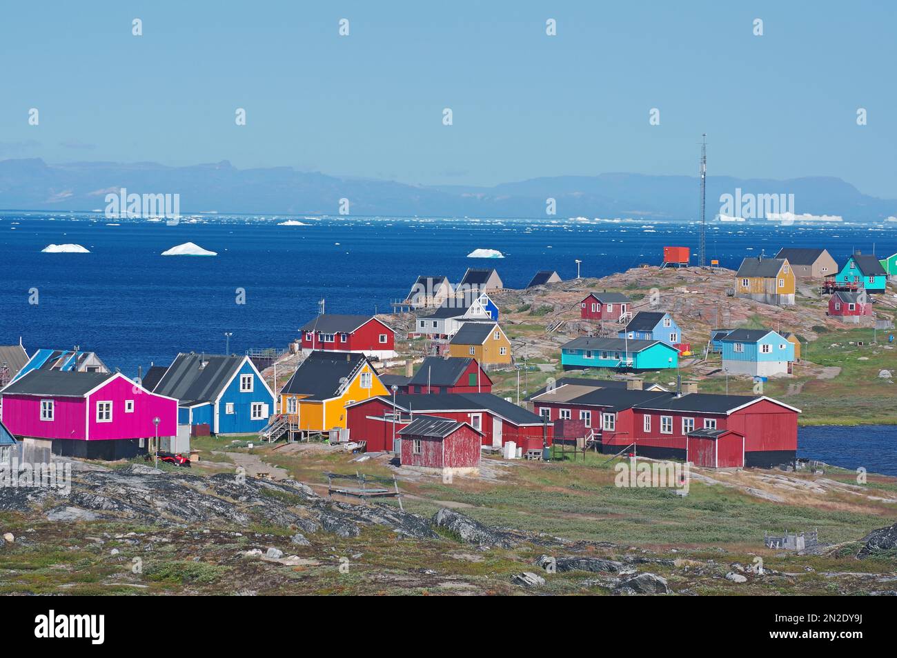 Different coloured wooden houses in front of the bay with icebergs ...