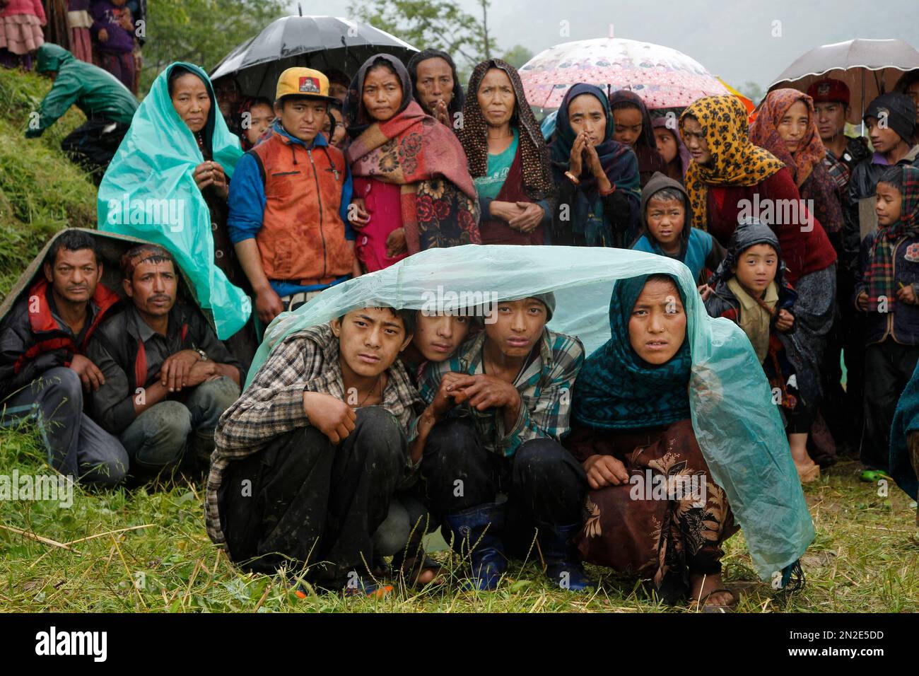 Villagers wait in the rain as an aid relief helicopter lands at their ...