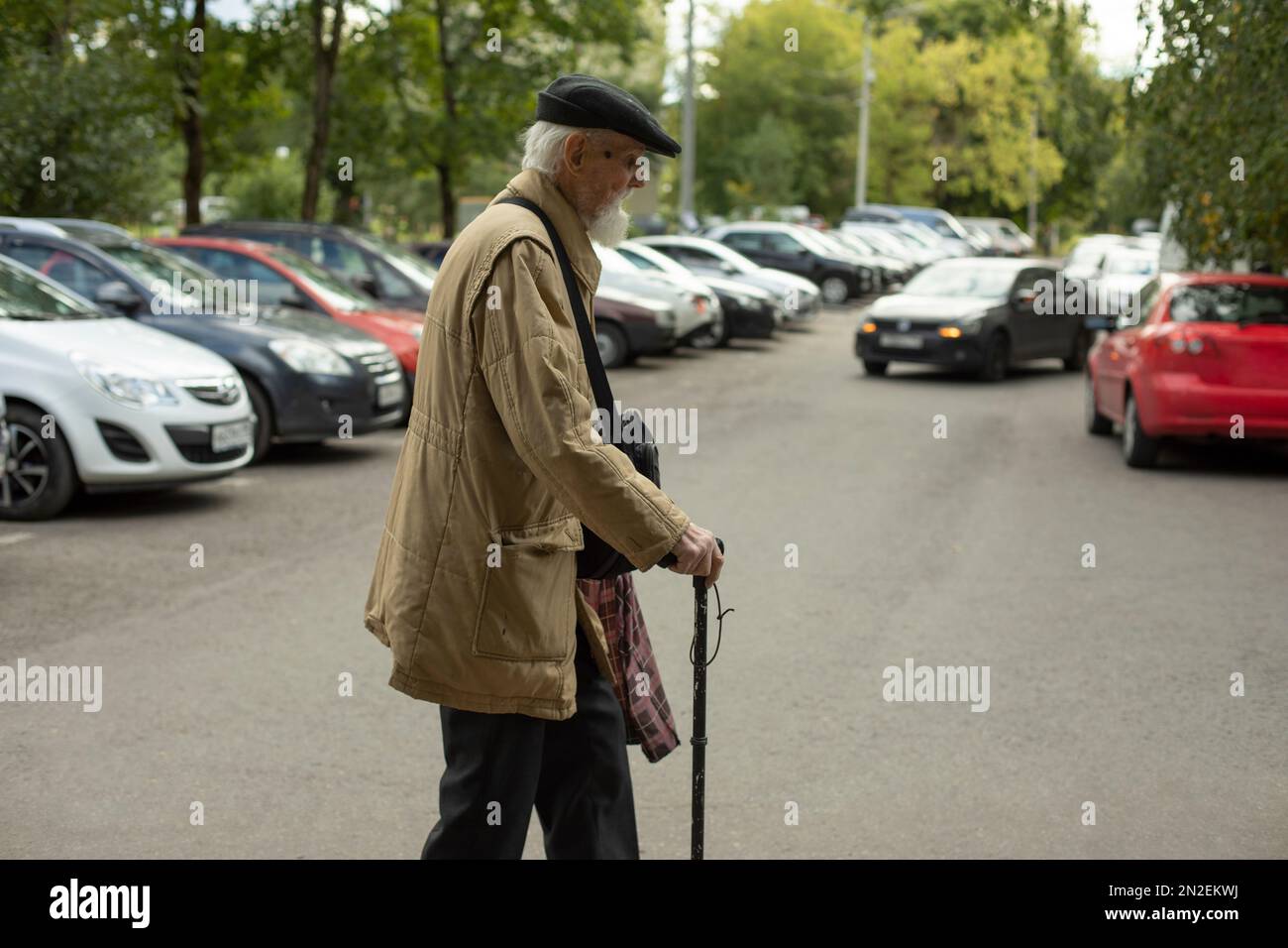 Old man walks through parking lot. Old man with stick. Man in poor ...