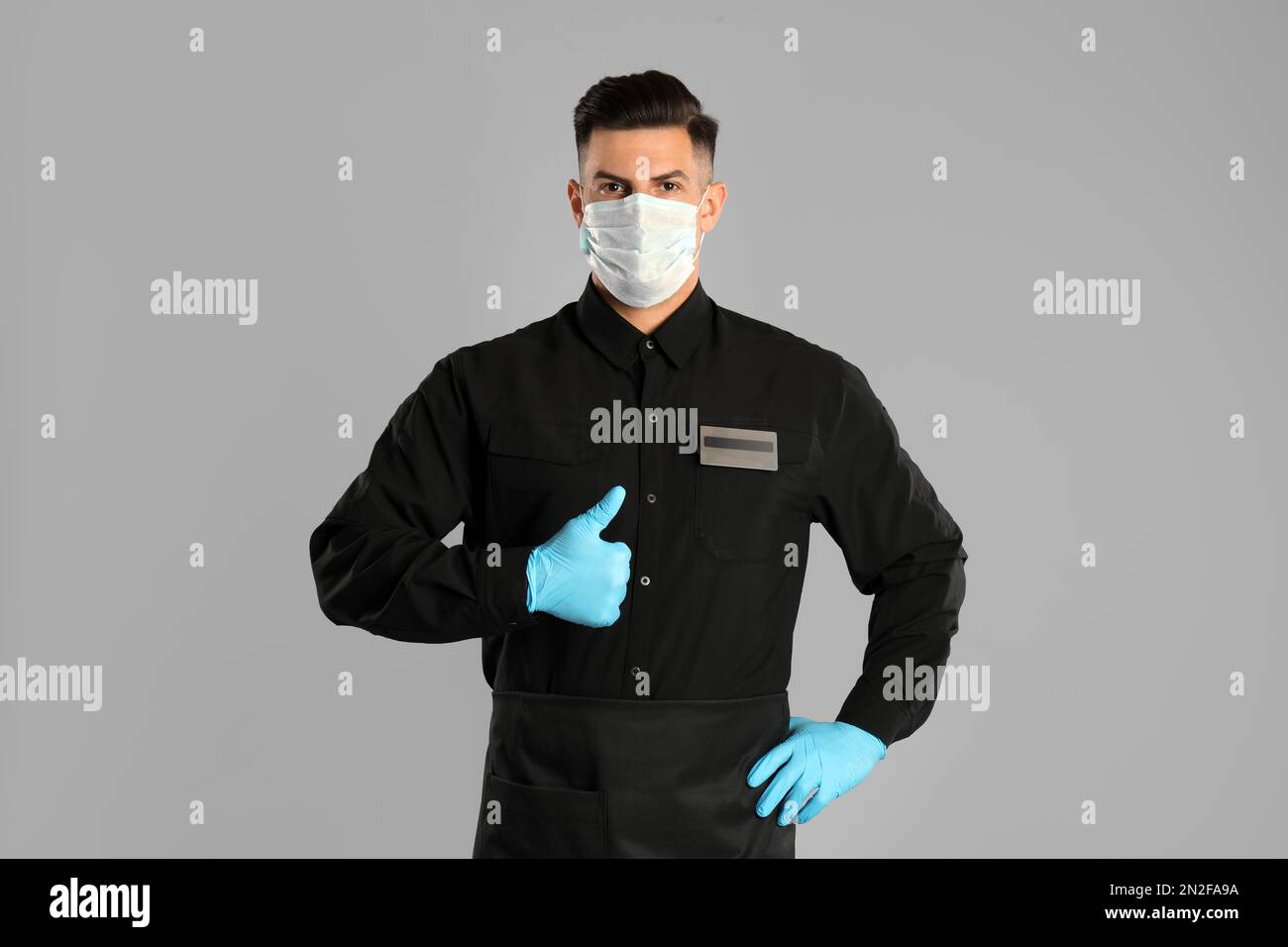 Waiter wearing medical face mask on light grey background Stock Photo ...