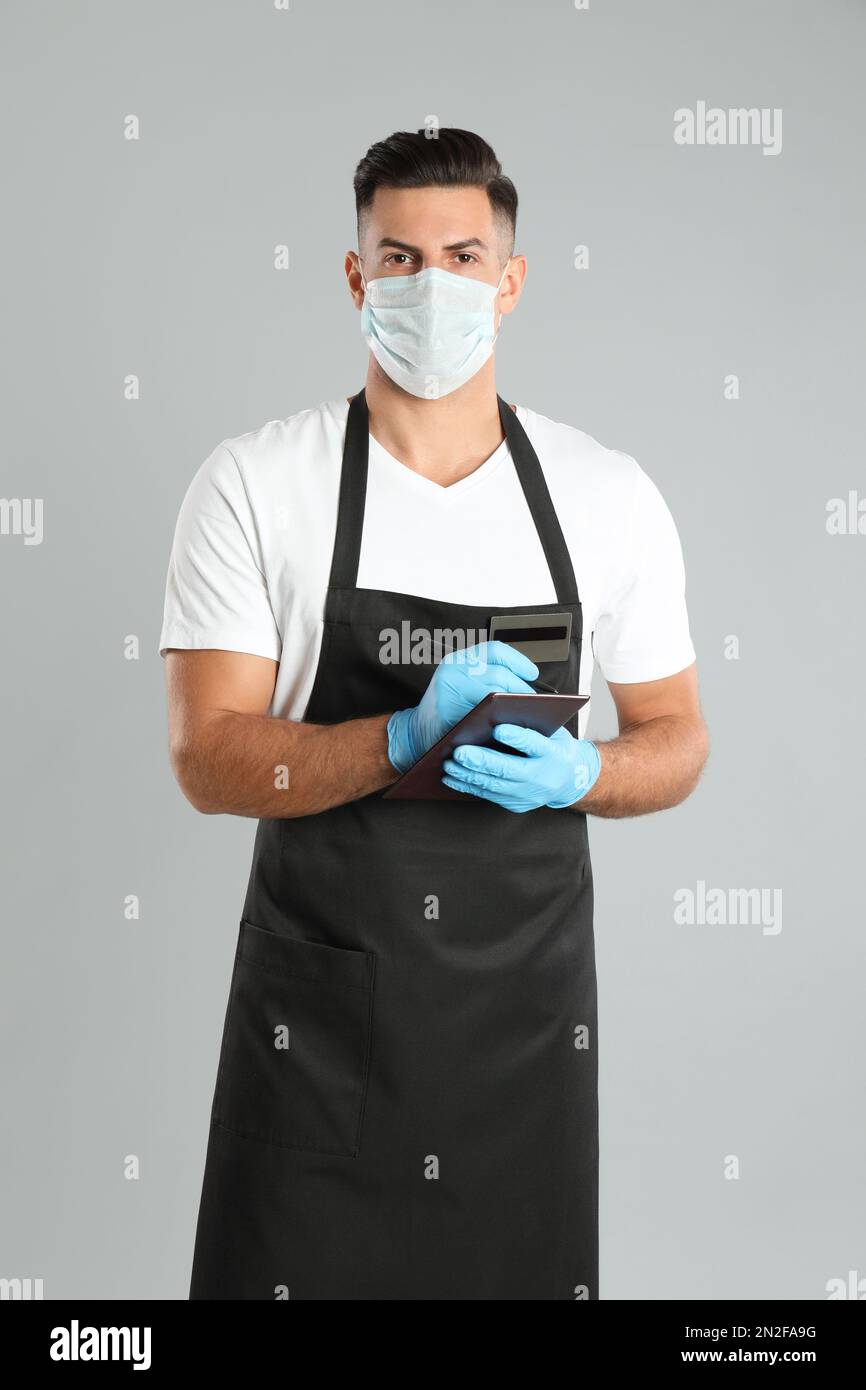 Waiter in medical face mask taking order on light grey background Stock ...