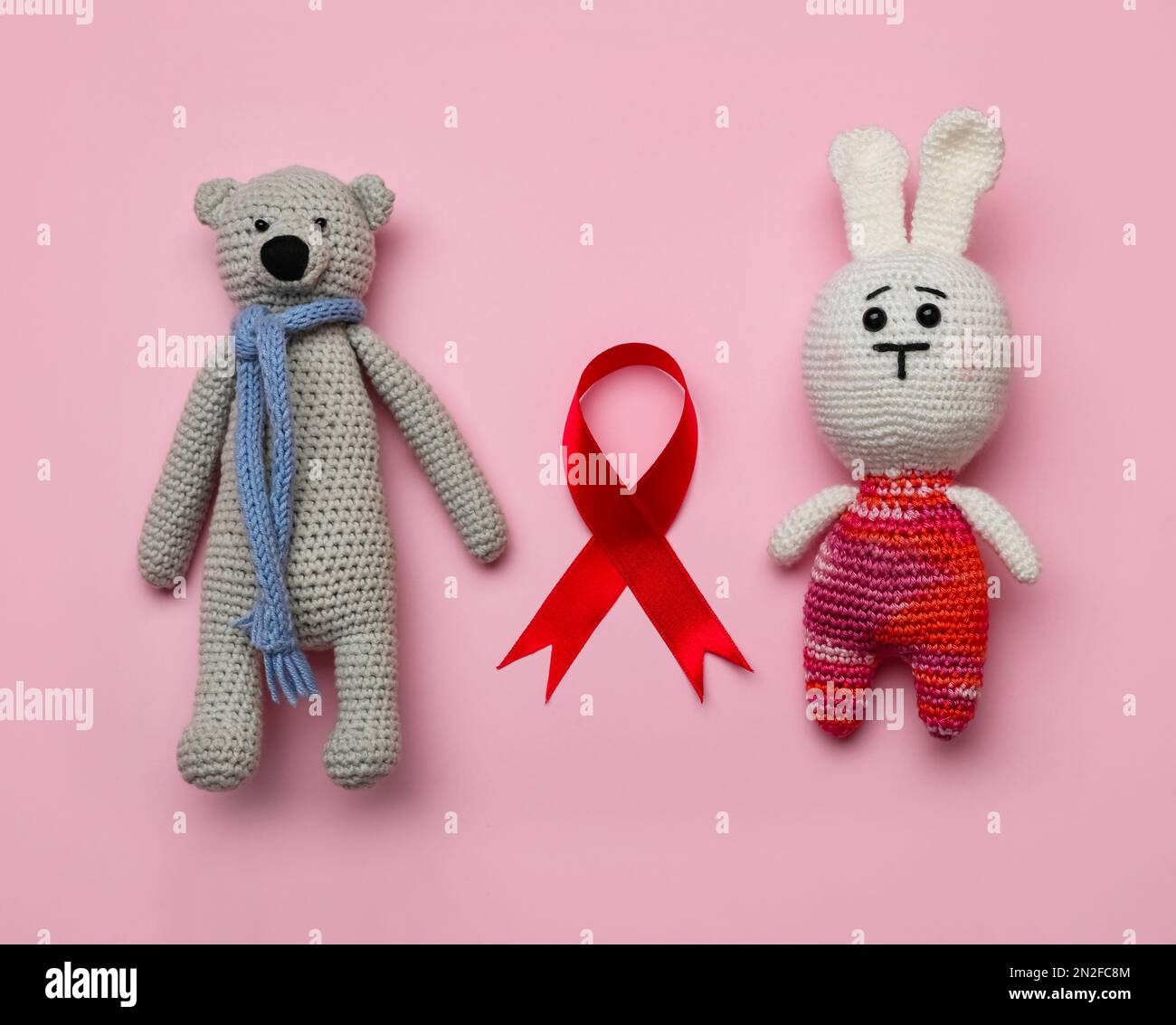 Cute knitted toys and red ribbon on pink background, flat lay. AIDS ...