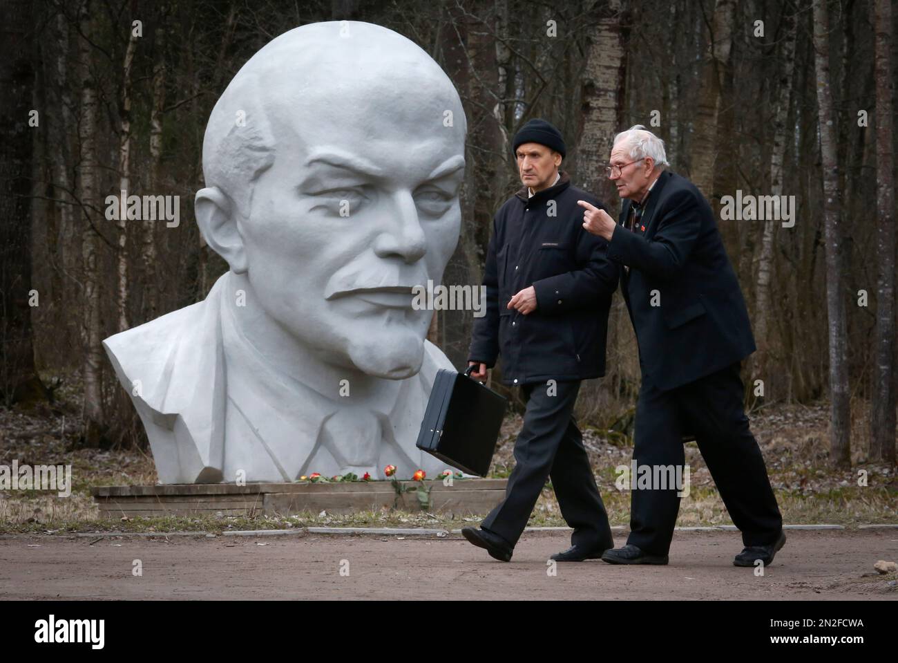 Russians walk past a statue of Soviet Union founder Vladimir Lenin ...