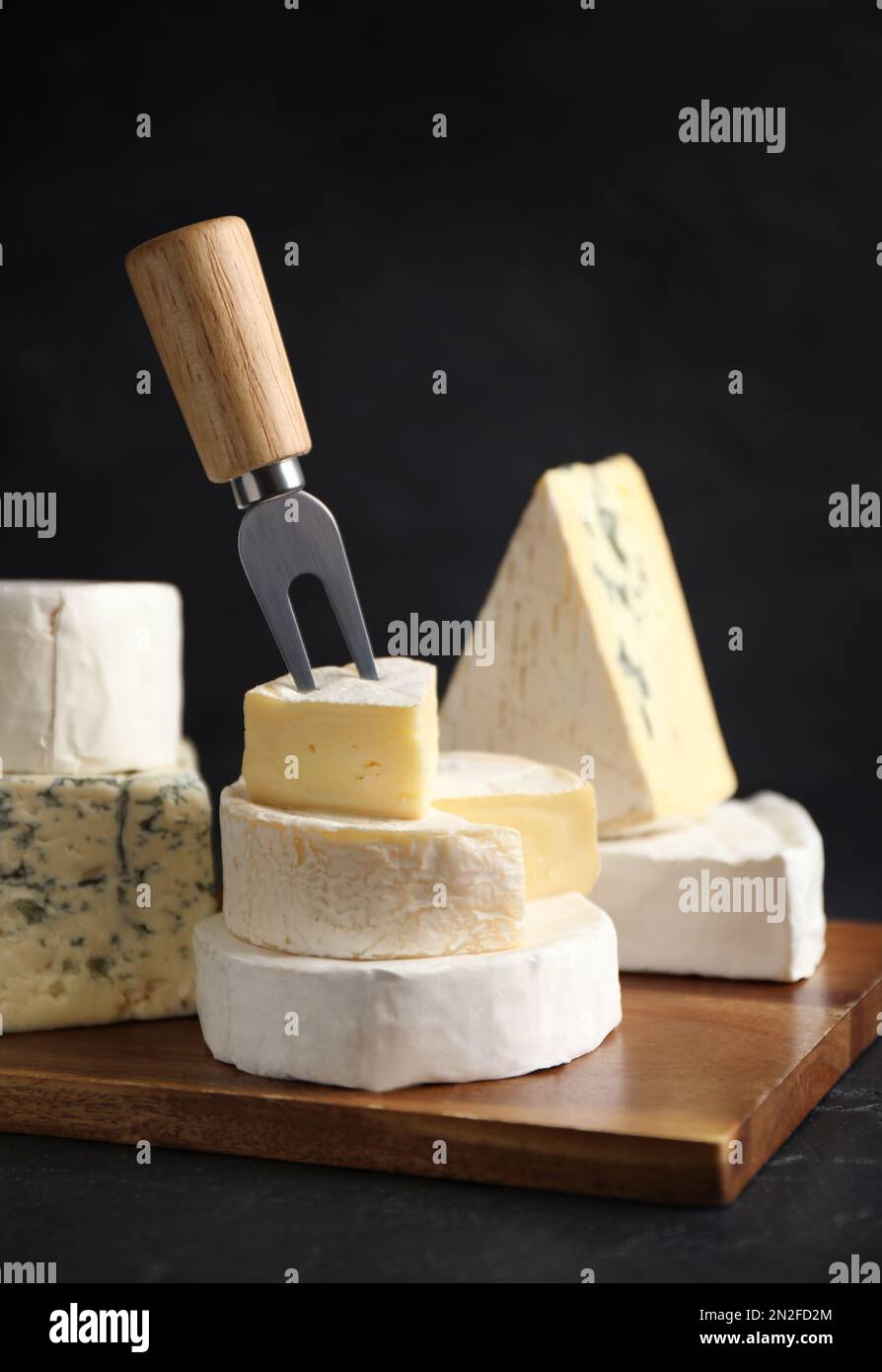 Different types of cheese and fork on black table Stock Photo - Alamy