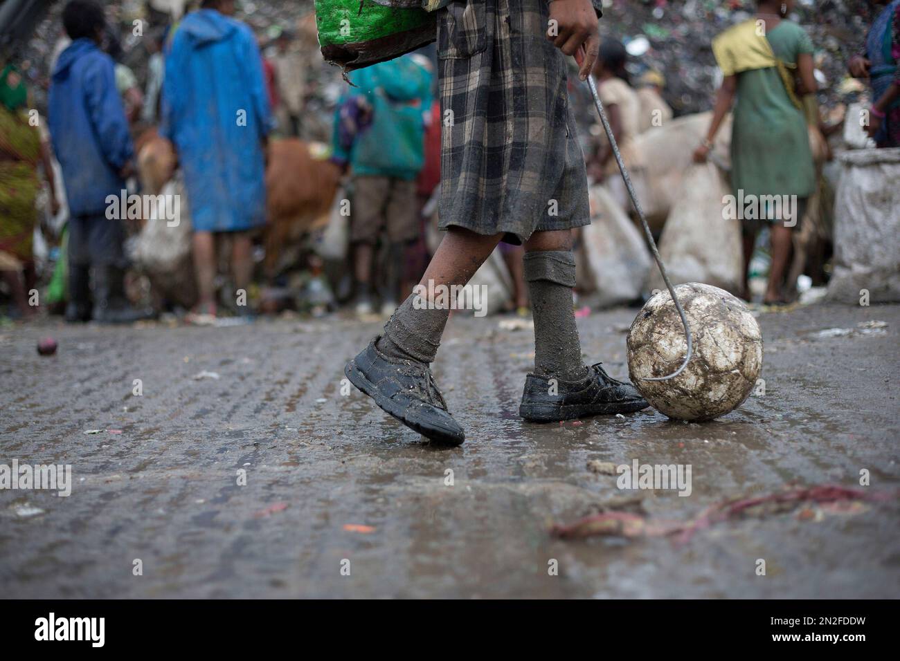 An Indian rag picker boy walks with a soccer ball he recovered from a ...