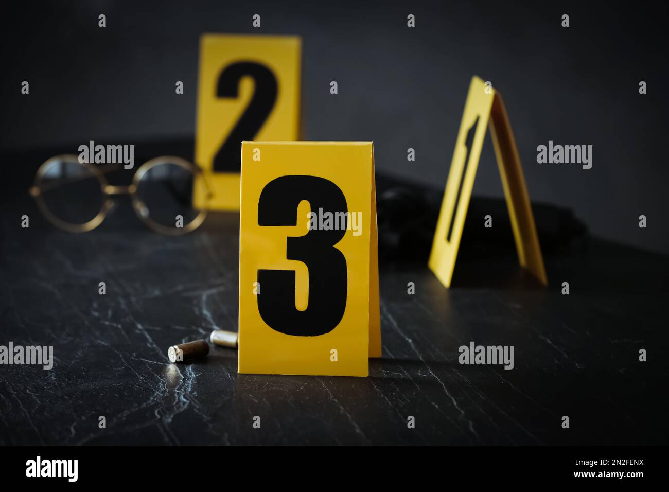 Shell casings and evidence marker on black slate table, closeup. Crime ...