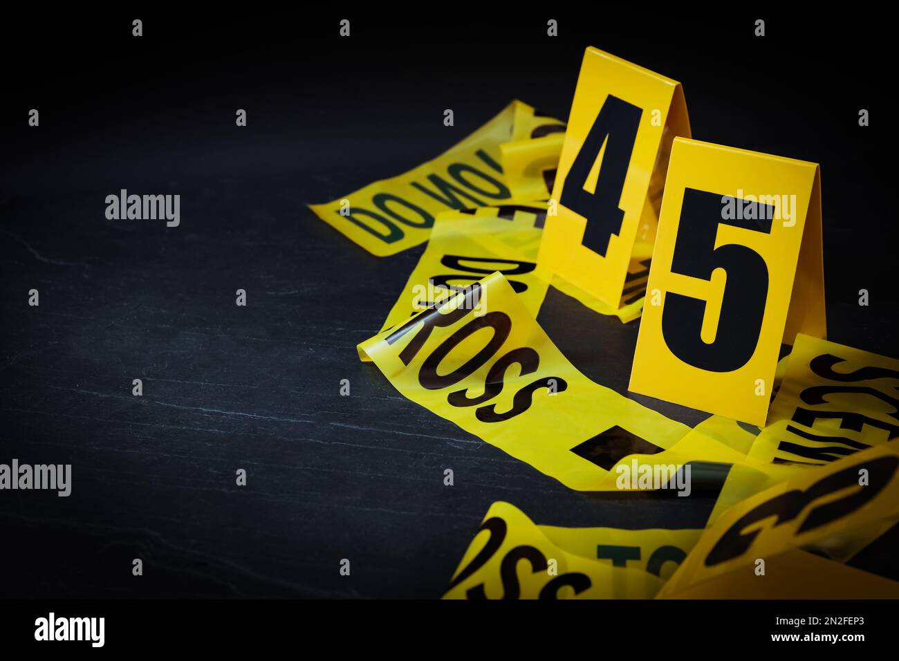 Crime scene tape and evidence markers on black slate background ...