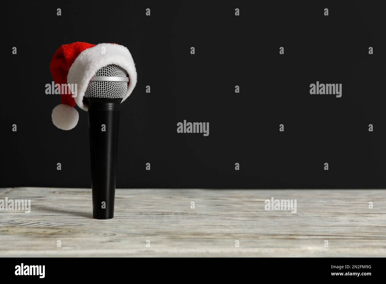 Microphone with Santa hat on white table against black background ...