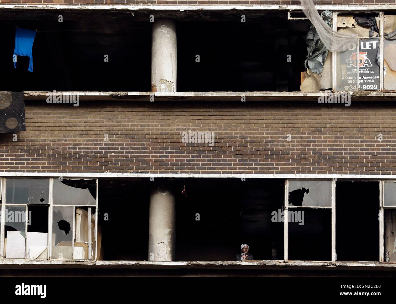 A man looks out from the window area of a dilapidated building occupied ...