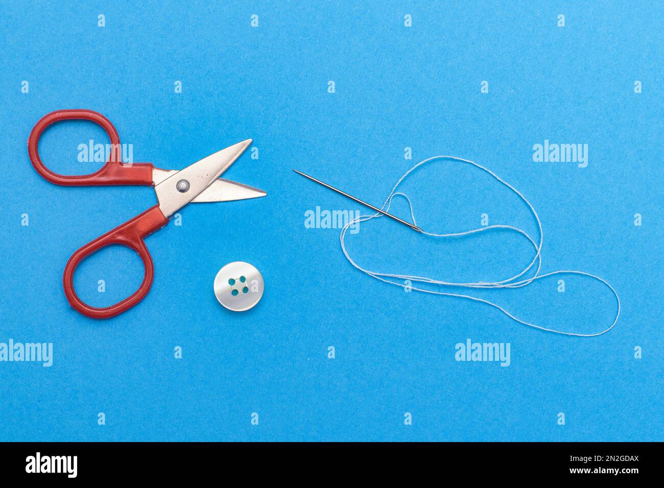 Needle scissors with thread and button on light blue background Stock ...