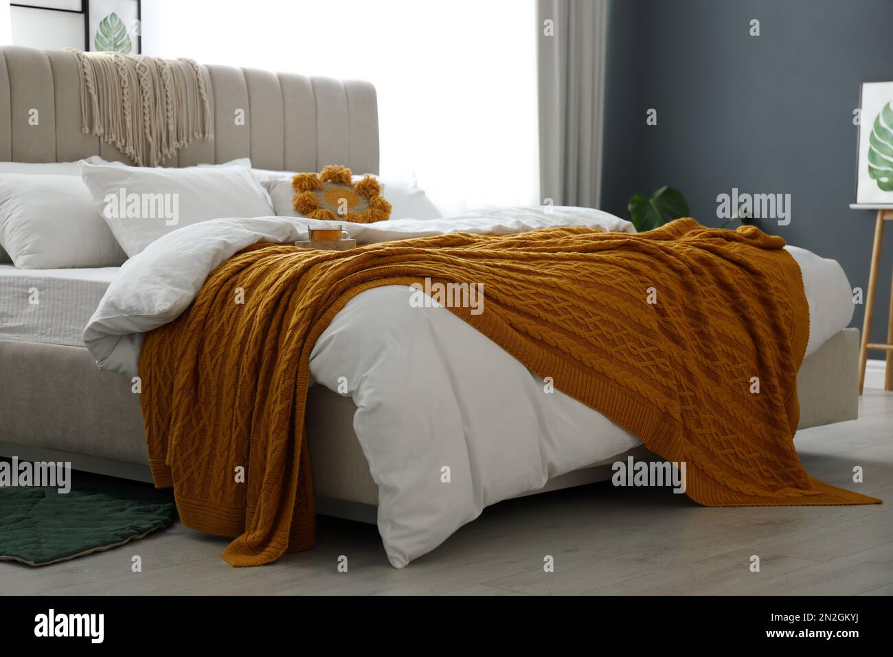 Comfortable bed with knitted orange plaid in stylish room interior ...
