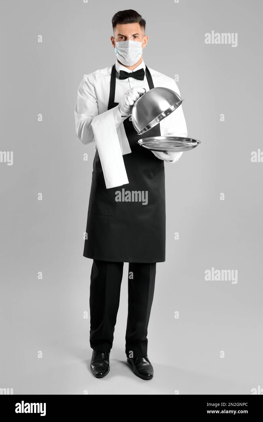 Waiter in medical face mask with empty tray on light grey background ...
