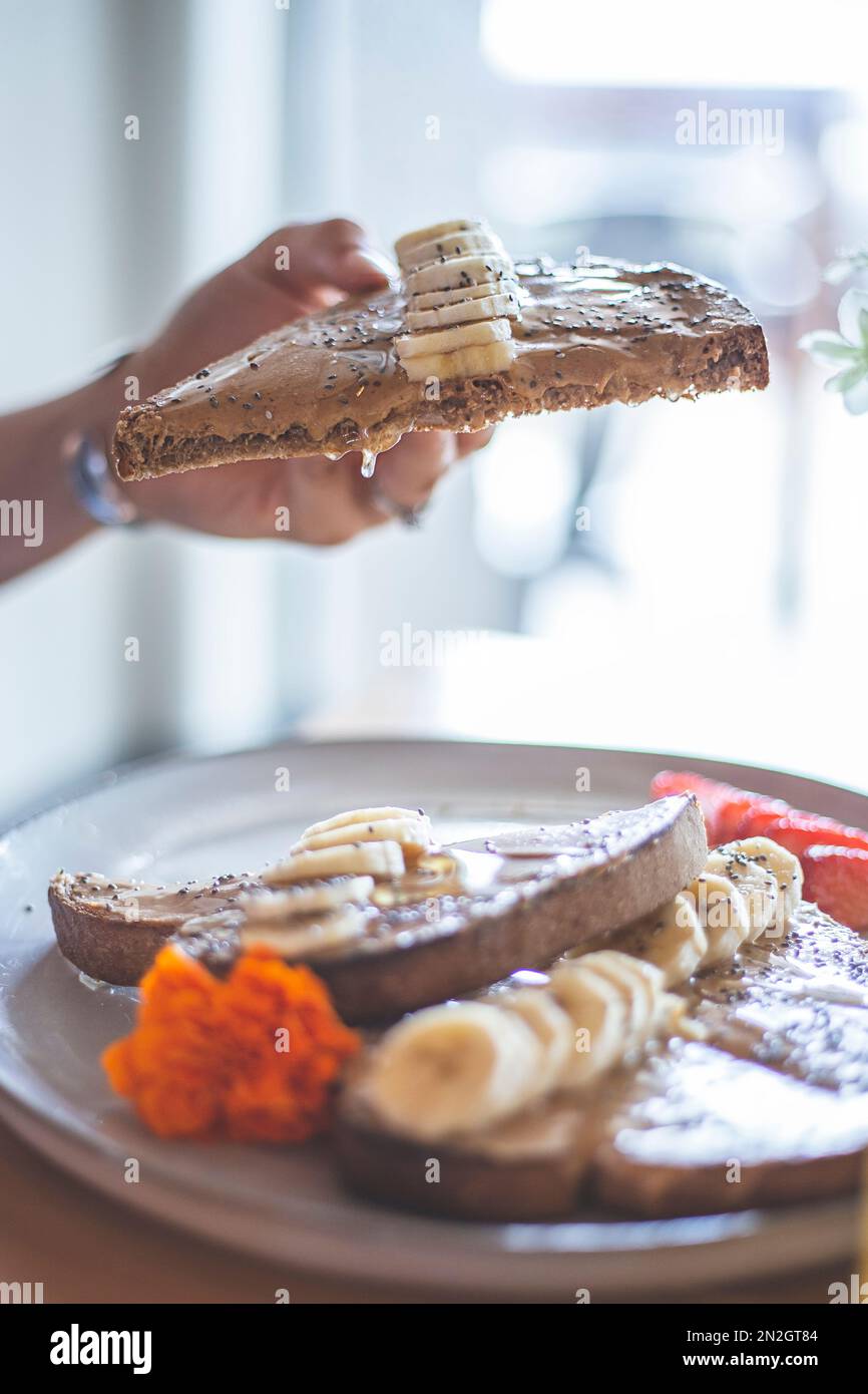 Woman's hand grabbing a peanut butter, banana and strawberry toast on a ...