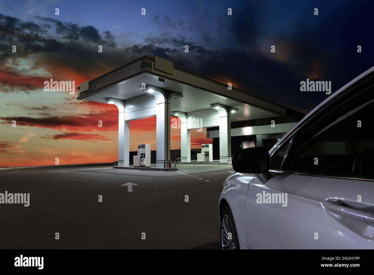 Car driving up to modern gas filling station beside the road in evening ...