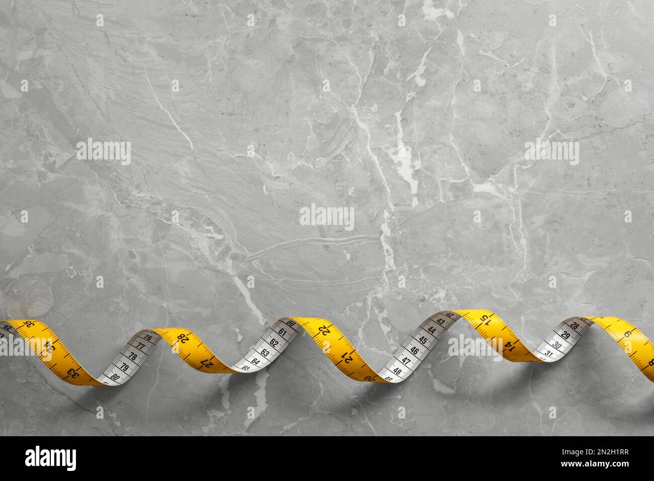 Measuring tape on light grey marble table, top view. Space for text ...