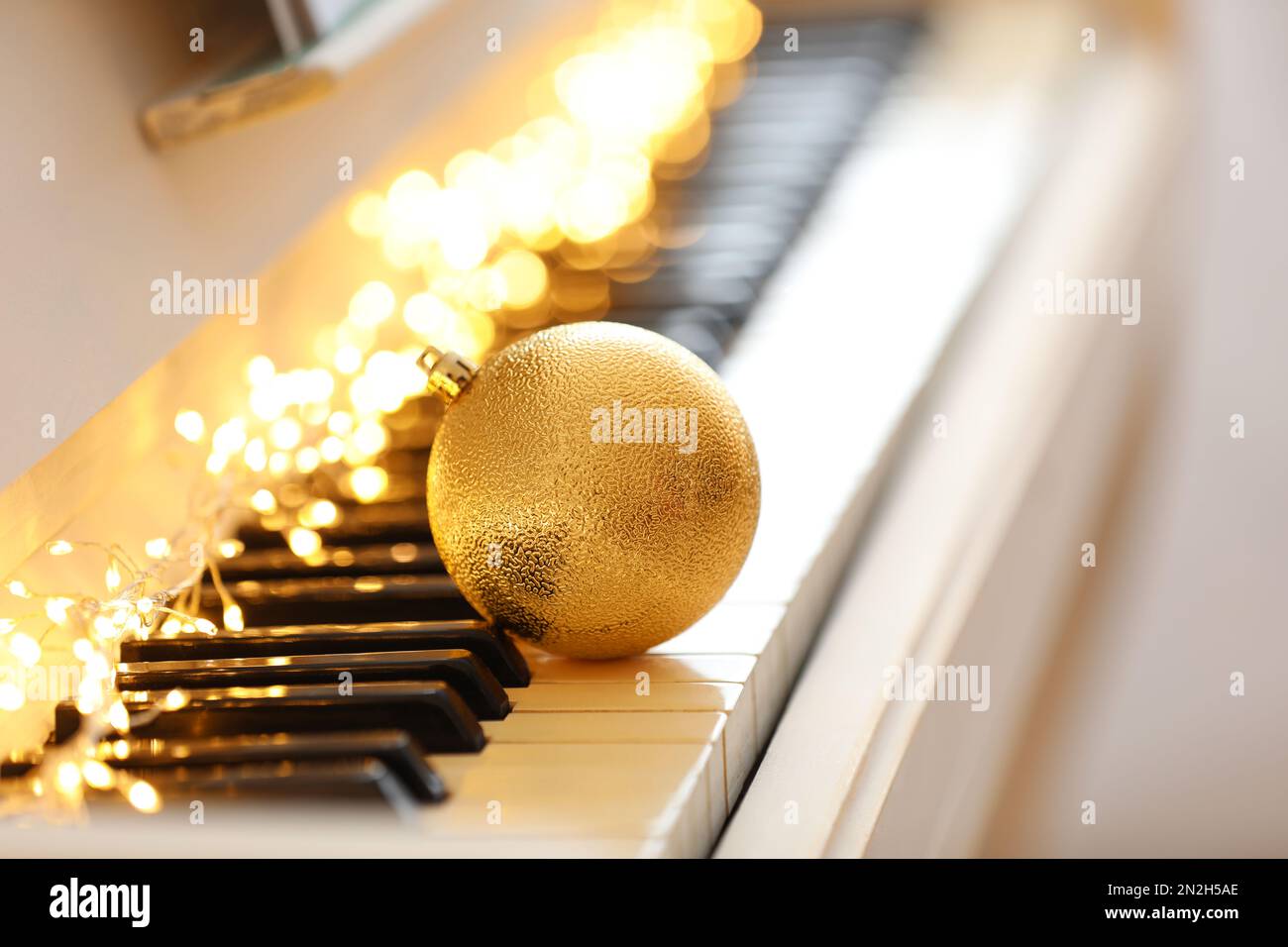 Beautiful golden bauble and fairy lights on piano keys, space for text ...