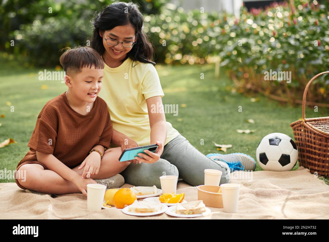 Smiling mother and son watching animated cartoon on smartphone when enjoying picnic Stock Photo ...