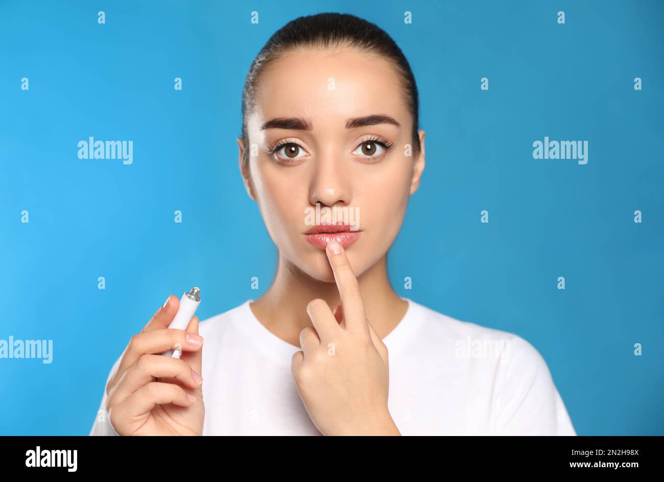 Woman with herpes applying cream on lips against light blue background ...
