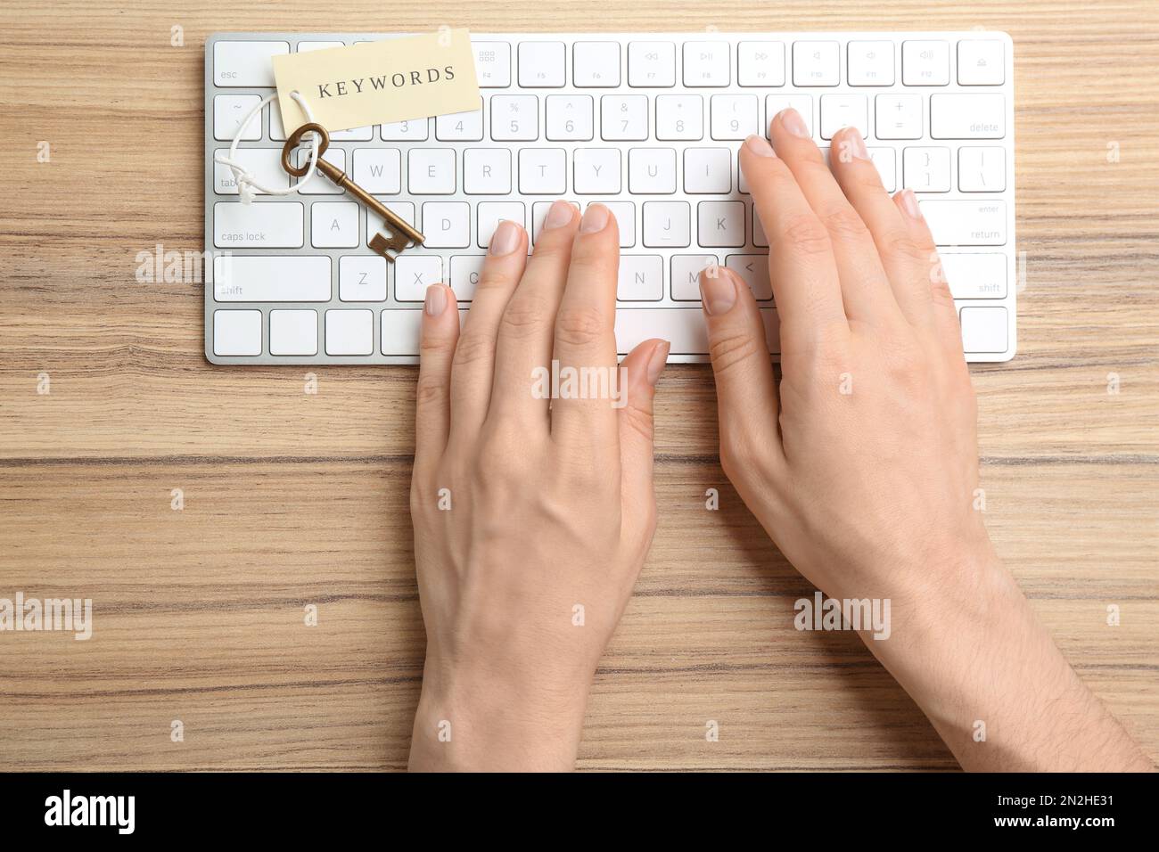 Woman typing on keyboard at wooden table, top view. Keyword concept ...