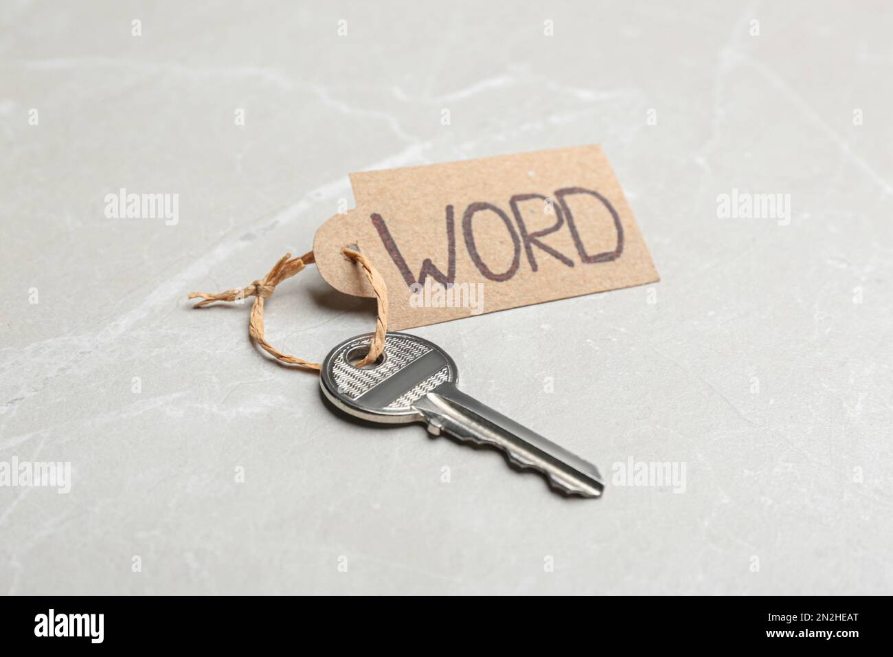Metal key with tag on light grey table. Keyword concept Stock Photo - Alamy