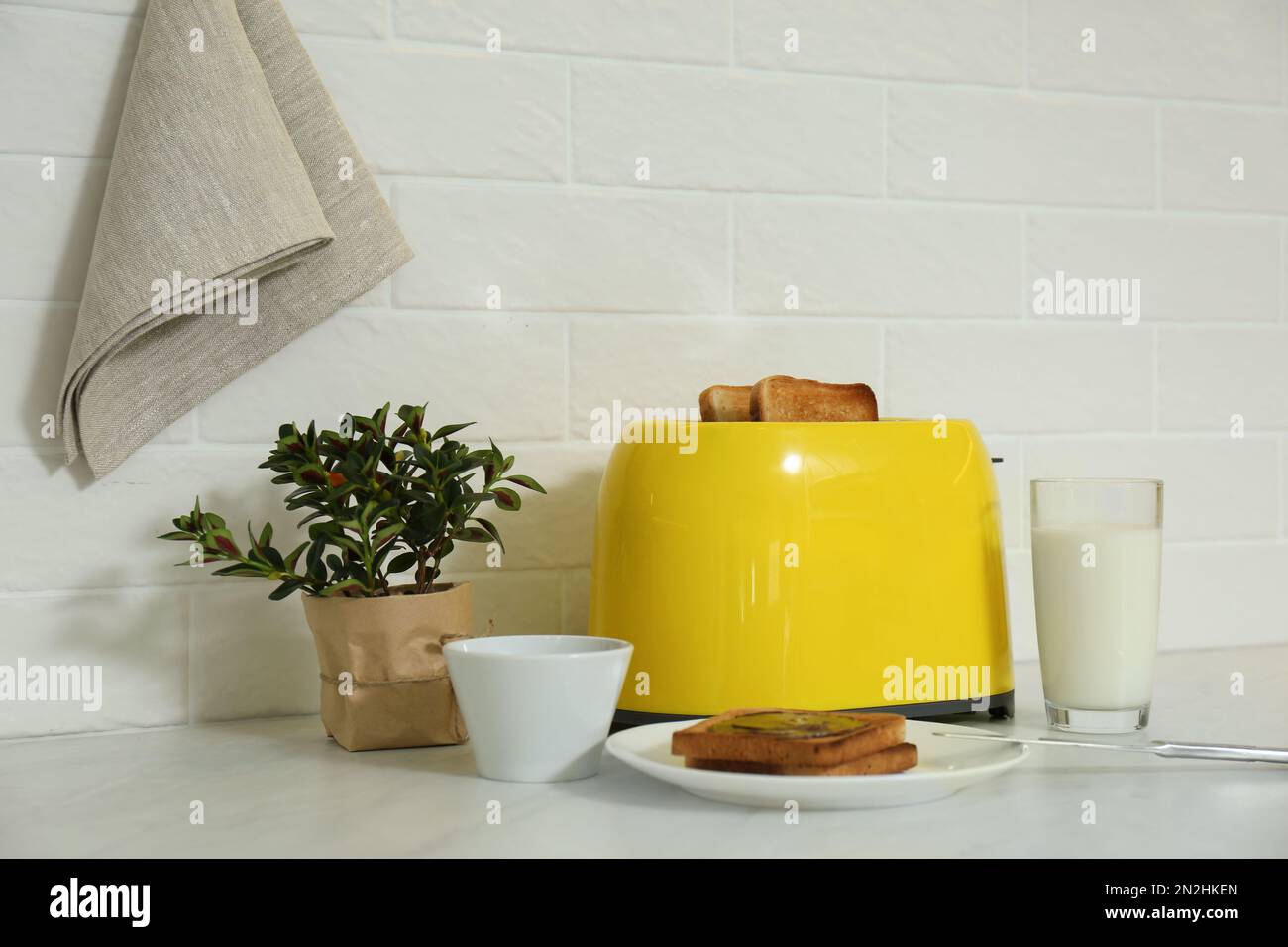 Modern toaster with bread slices, glass of milk and plant on white table in kitchen Stock Photo ...