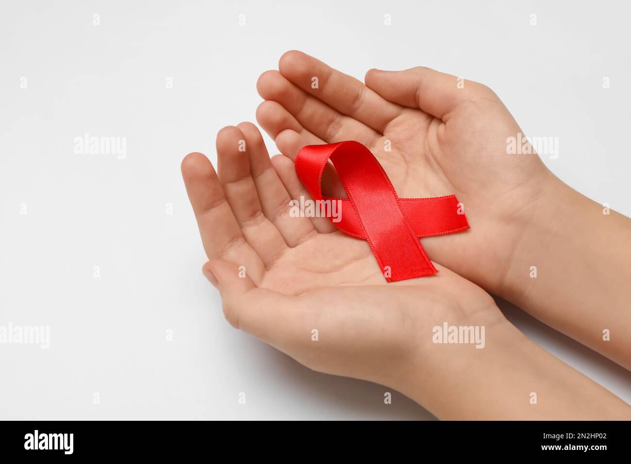 Little girl holding red ribbon on white background, closeup. AIDS ...