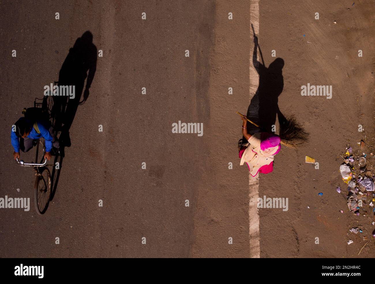 An Indian civic worker sweeps a street as a man on bicycle heads to ...