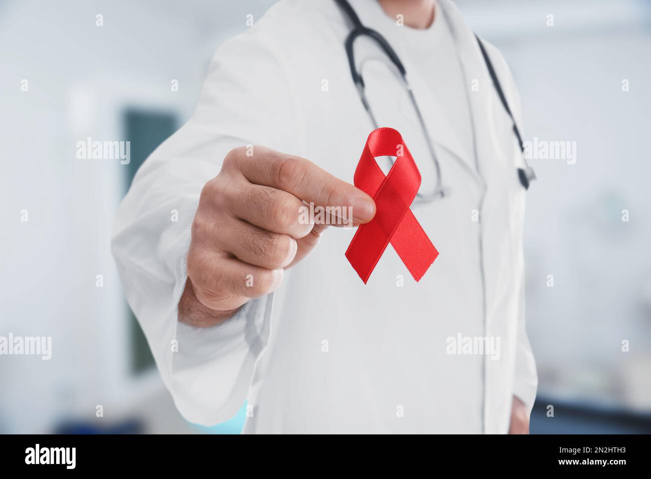Doctor holding red awareness ribbon on blurred background, closeup ...