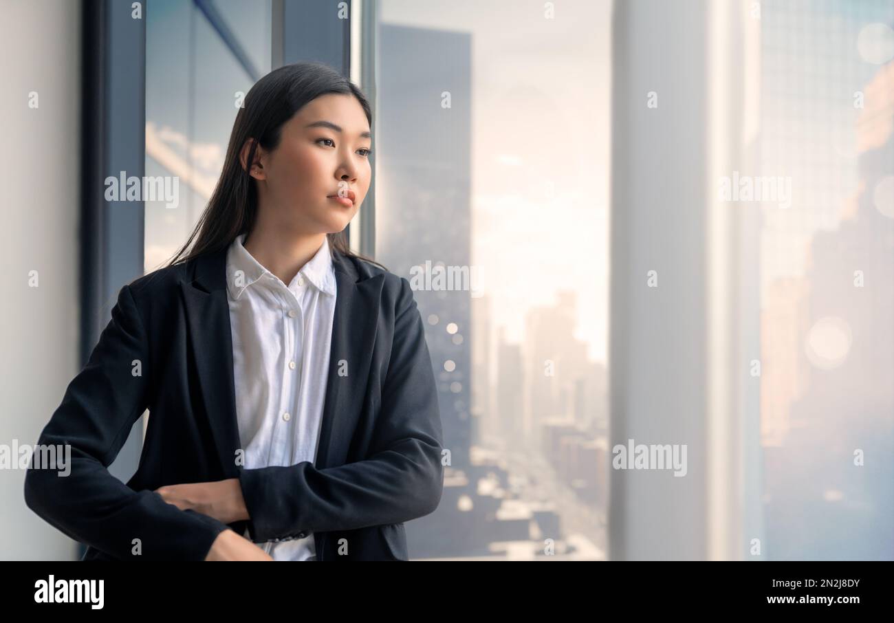 Young asian woman standing near window with uncertainty while thinking ...