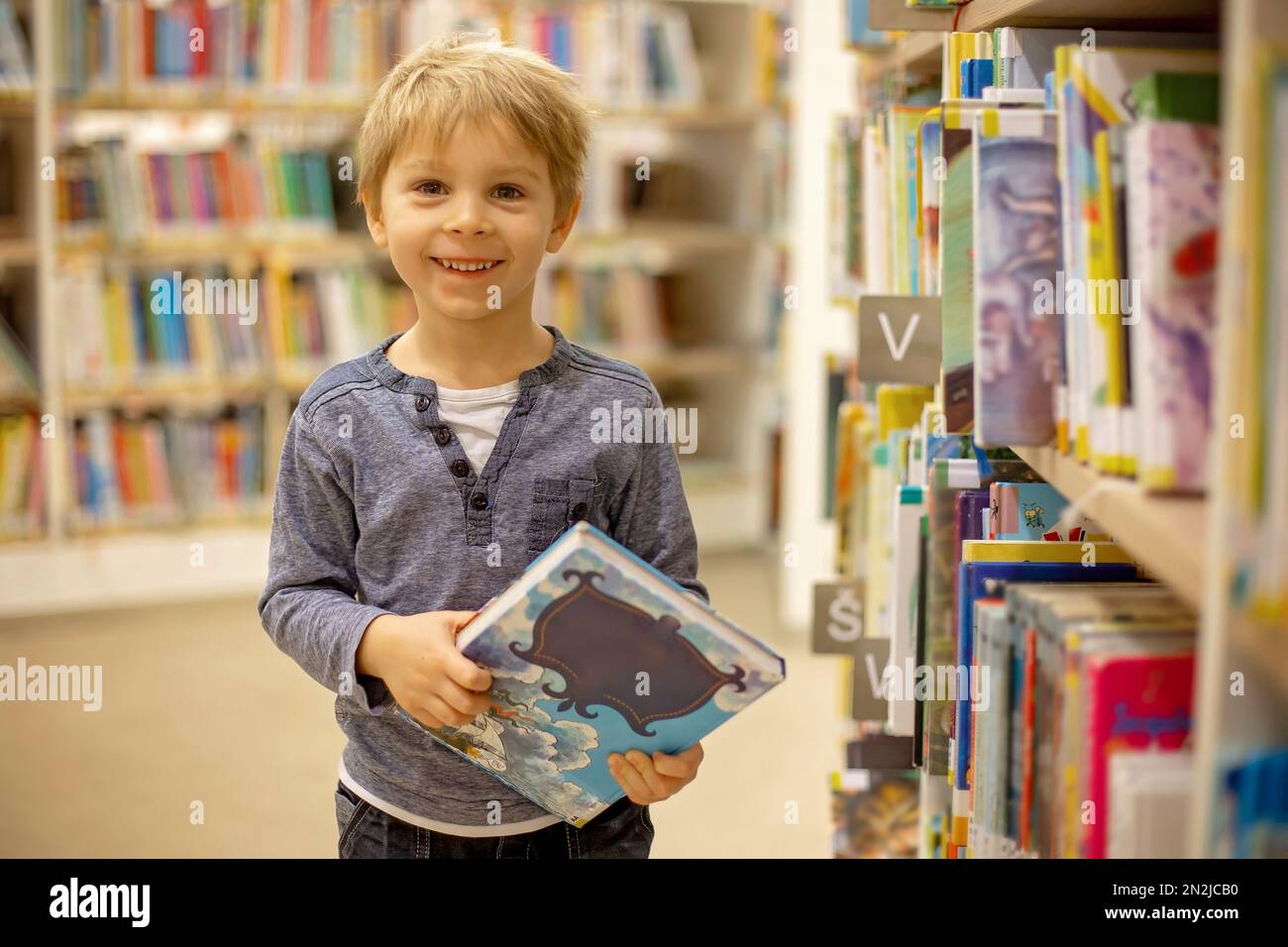 Adorable little child, boy, sitting in library, reading book and ...