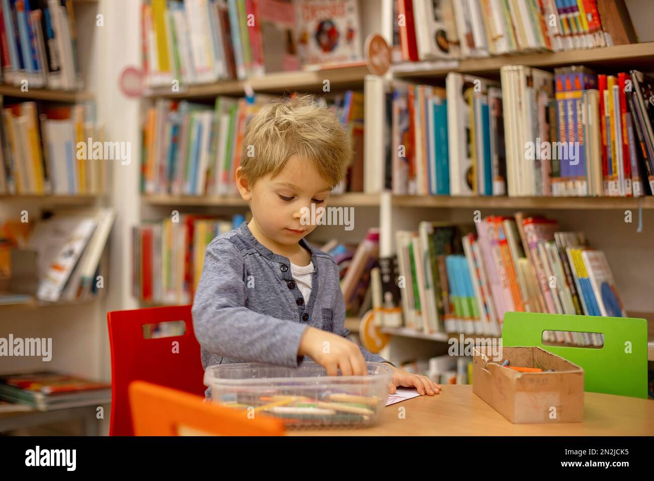Adorable little child, boy, sitting in library, reading book and ...