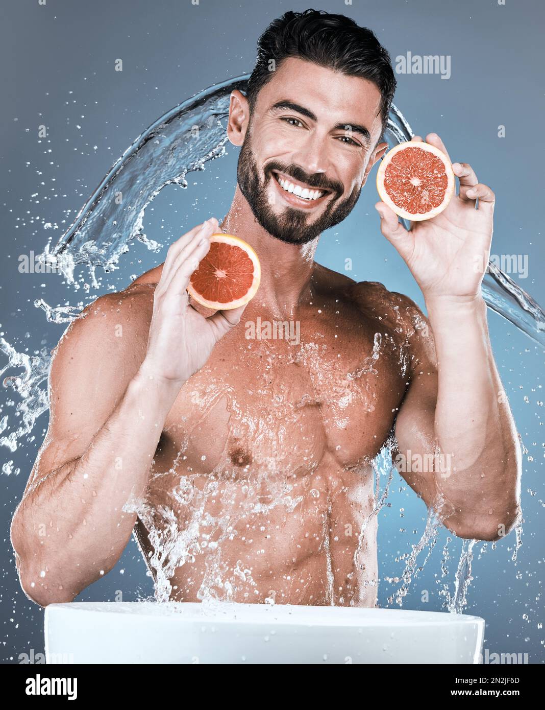 Portrait, water splash and man with grapefruit in studio isolated on a blue background. Skincare ...