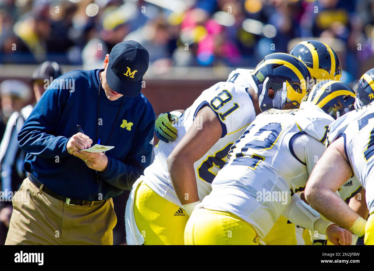Michigan head coach Jim Harbaugh, left, leans in to listen and take ...