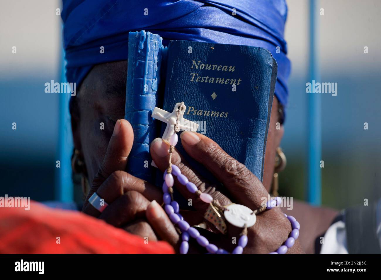 A woman holds a copy of the New Testament, a candle and a rosary in ...