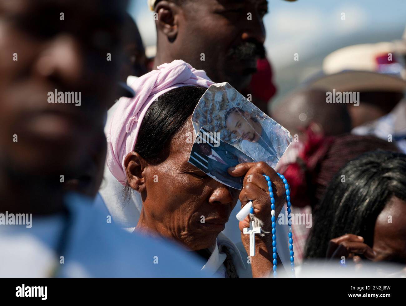 A woman prays, holding a rosary and pictures of her relatives, during a ...