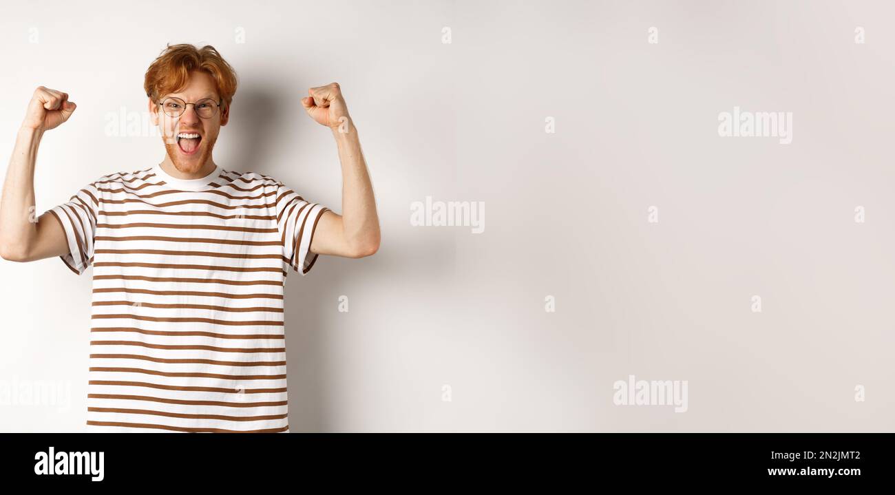 Joyful redhead guy raising hands up like winner, winning prize and ...
