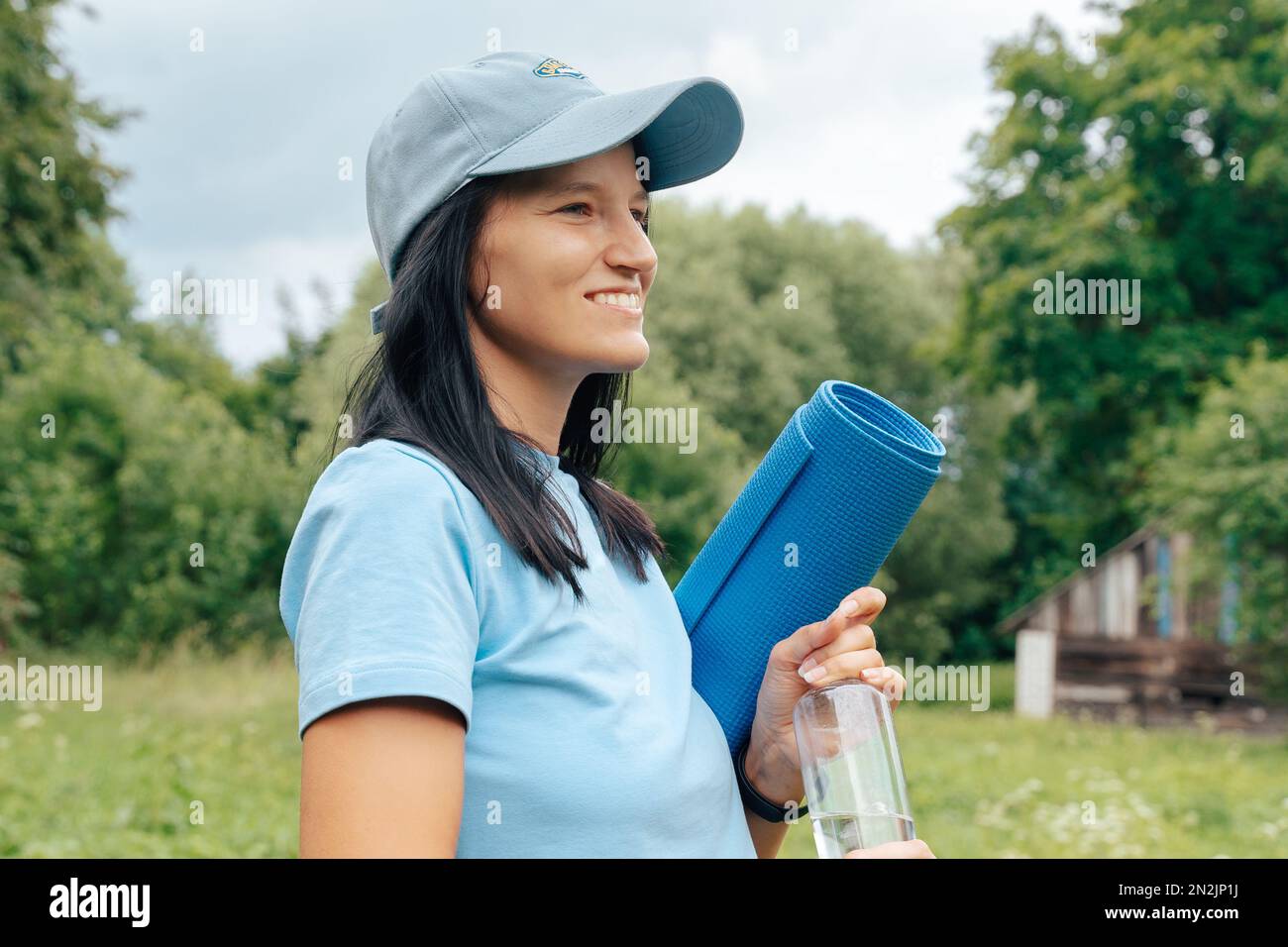 Beautiful smile millennial woman hold water bottle yoga mat. Fitness female walking outdoor ...