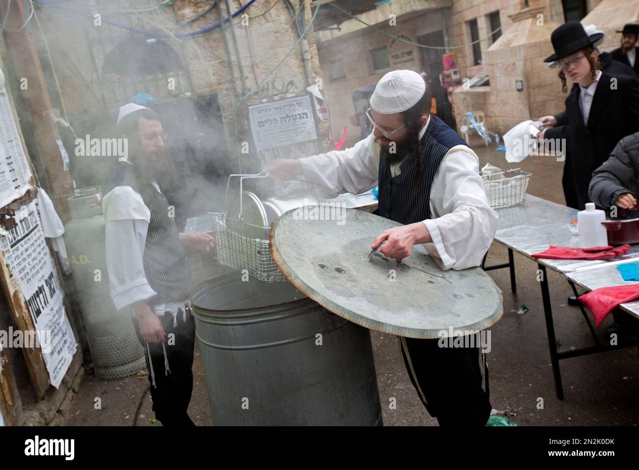 Ultra-Orthodox Jewish men dip a basket with kitchen items into boiling ...
