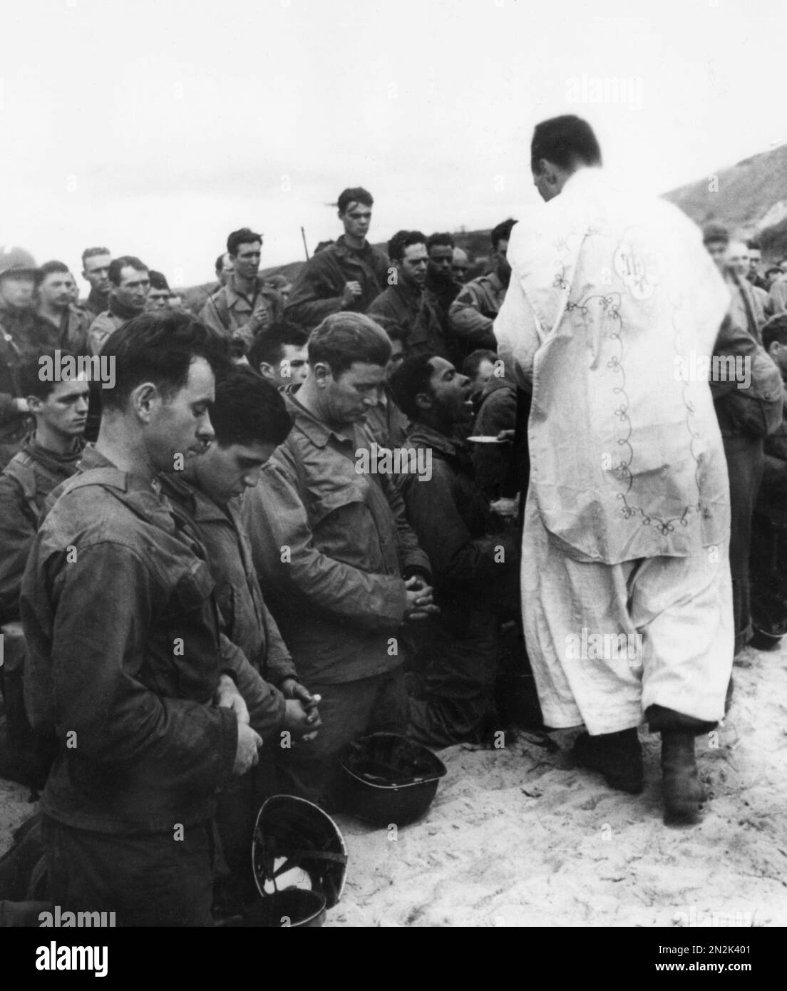 A catholic priest passes along the line of kneeling US troops during a ...