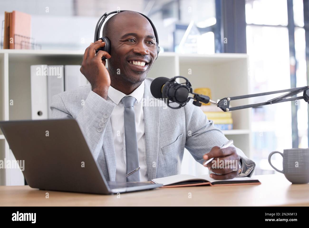 News, laptop and radio with a black man presenter writing in a notebook ...
