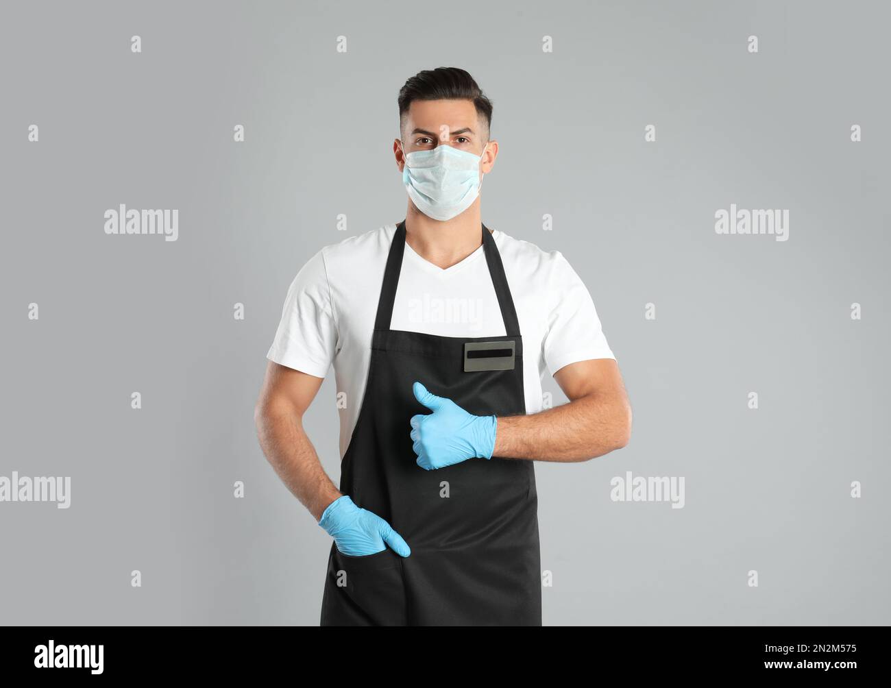 Waiter wearing medical face mask on light grey background Stock Photo ...