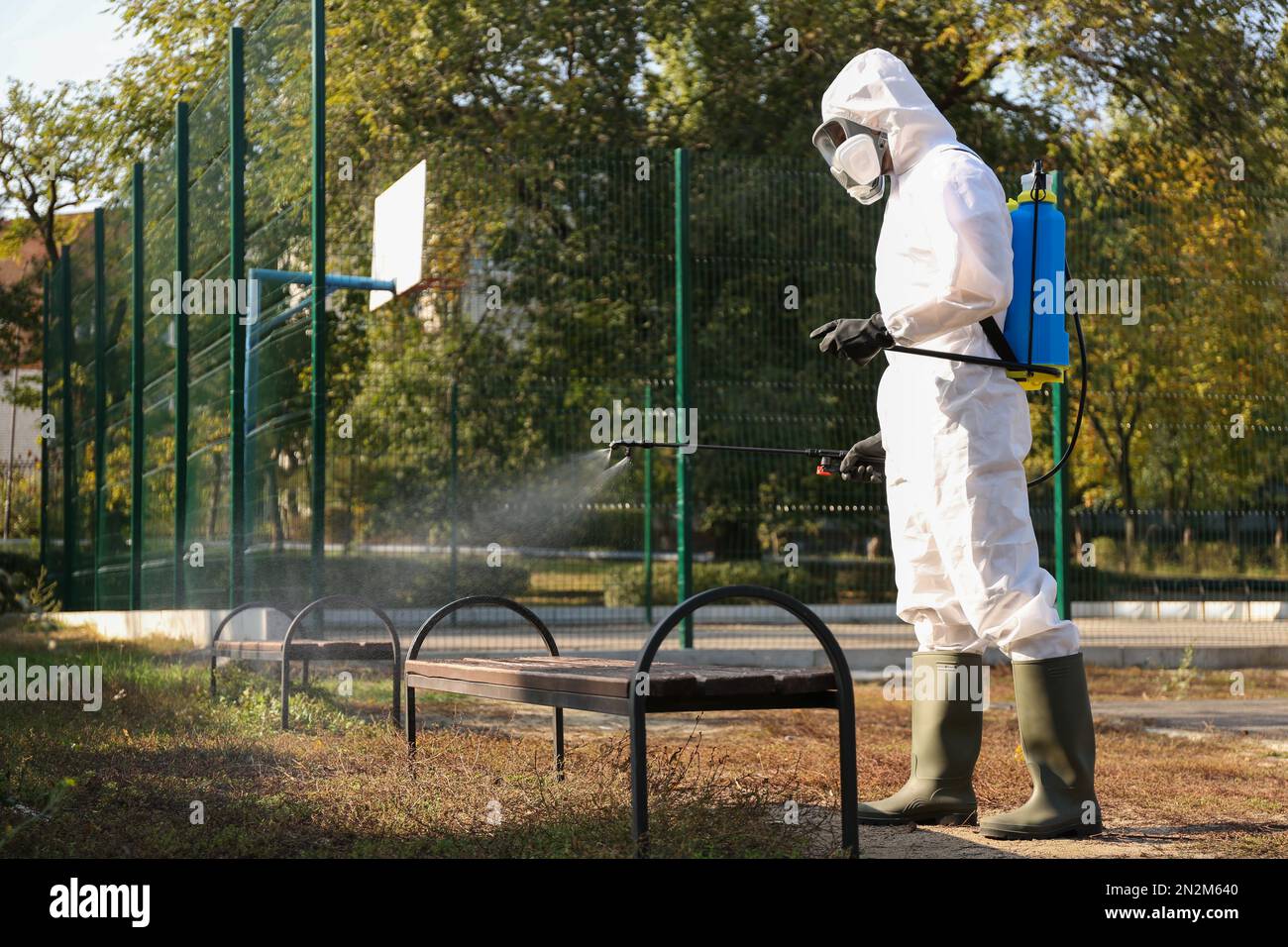 Person in hazmat suit spraying disinfectant onto bench outdoors ...